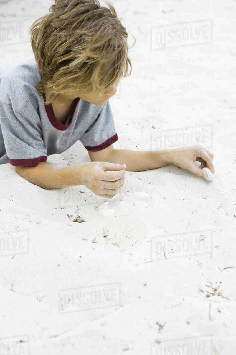 Boy lying on the ground, arranging pebbles in sand - Royalty-free Stock ...