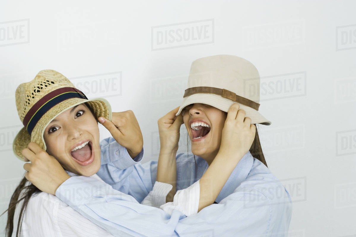 Two young friends pulling hats over each other's faces and smiling, one ...