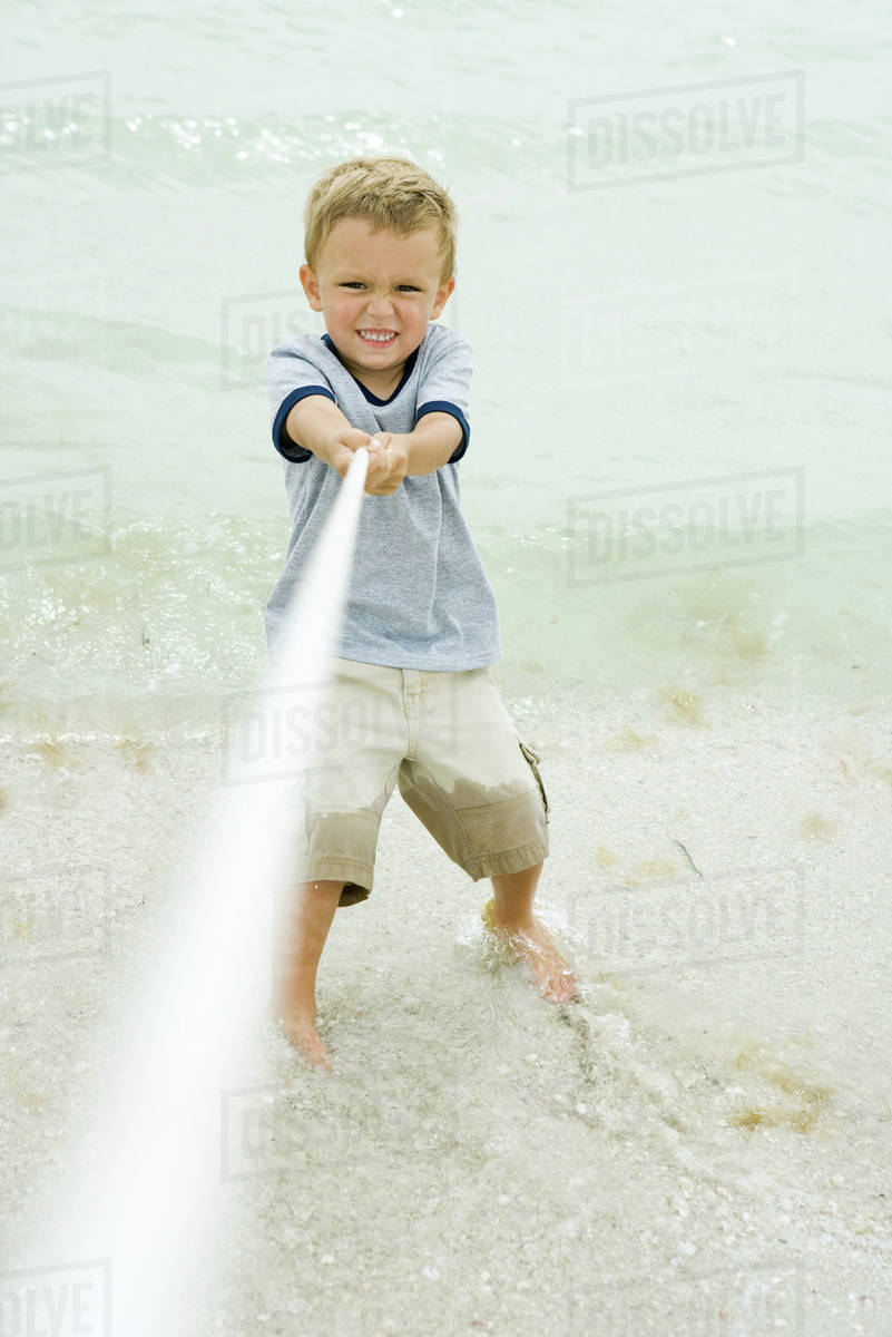 Little boy pulling on rope, making face, on beach - Stock Photo - Dissolve