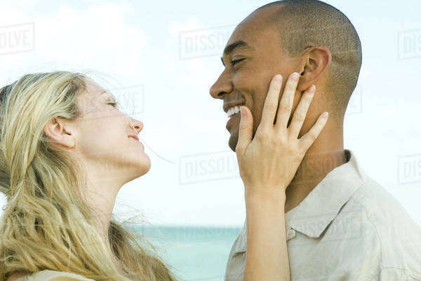 Couple smiling at each other, woman's hand on man's cheek, side view ...