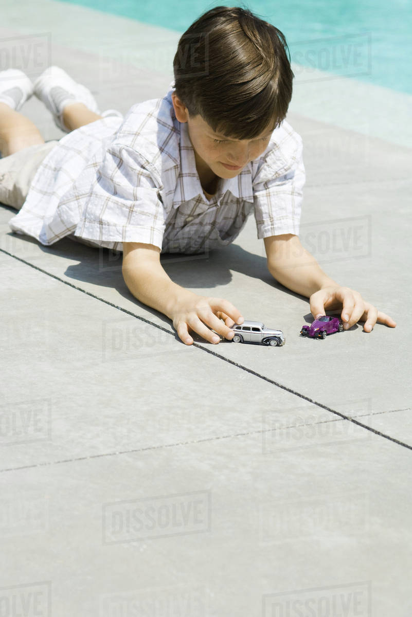 Boy lying on ground, playing with toy cars, next to pool - Royalty-free ...
