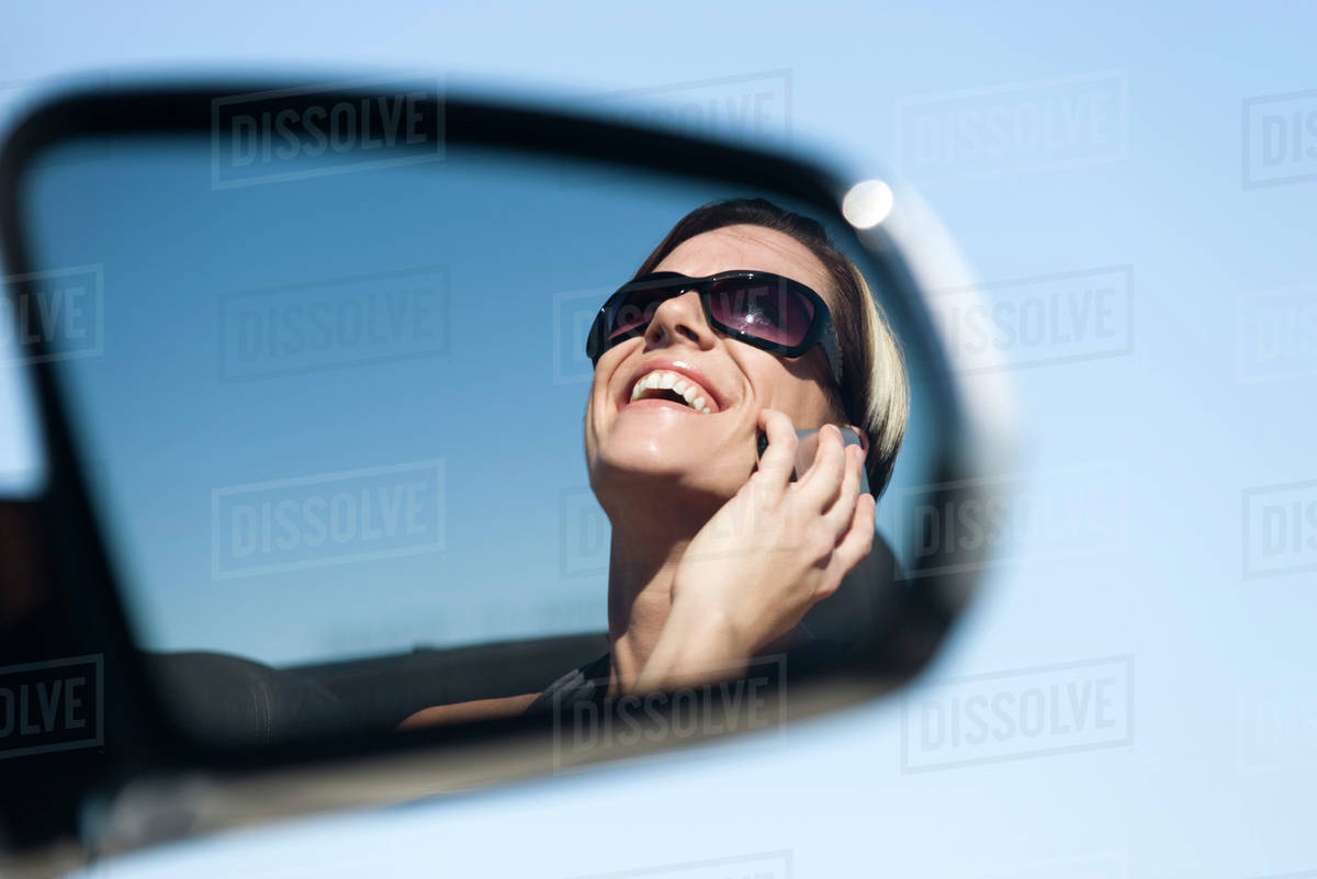 Woman talking on cell phone, reflection in side-view mirror - Royalty ...