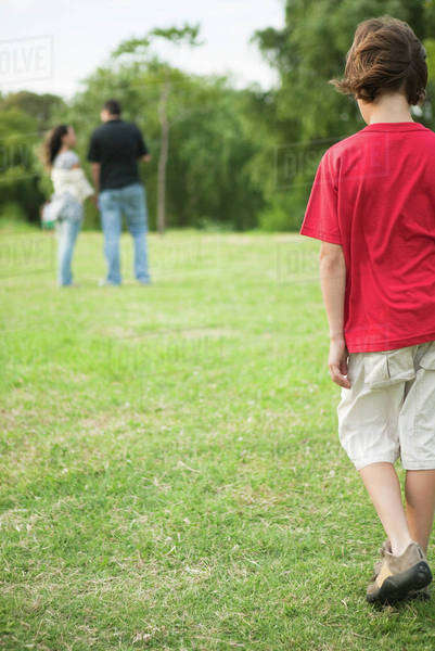Boy walking sulkily toward parents having conversation distance - Stock ...