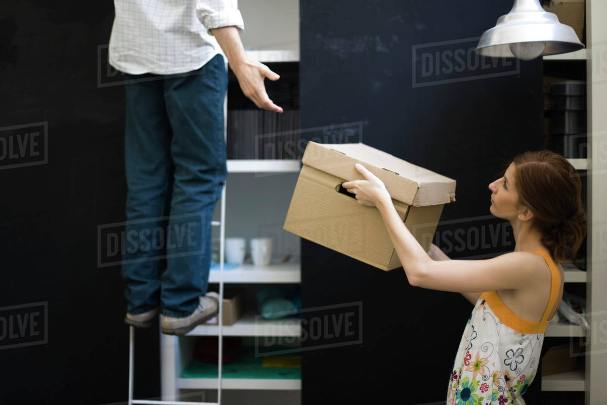 Woman handing box to man standing on ladder - Royalty-free Stock Photo ...
