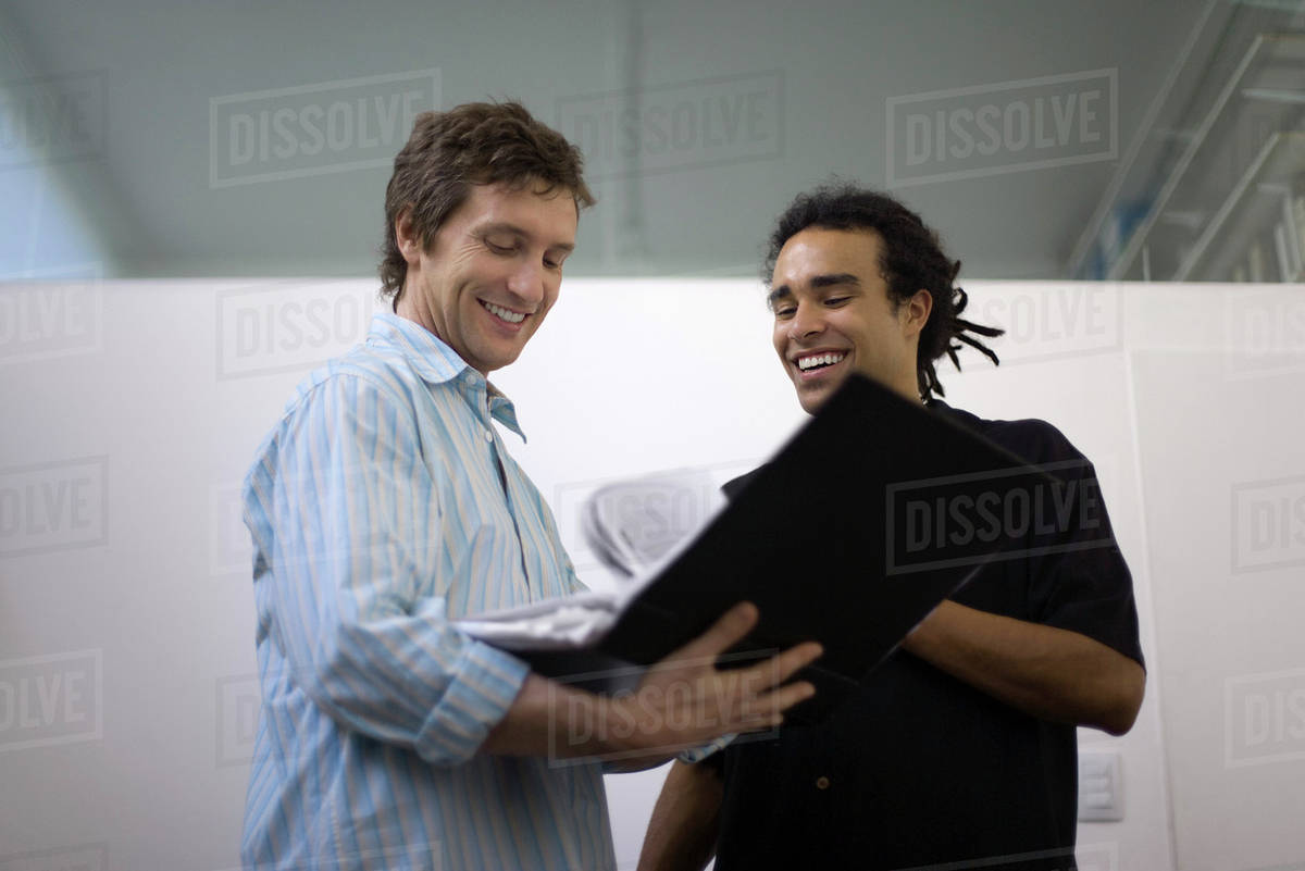 Men flipping through binder together - Stock Photo - Dissolve