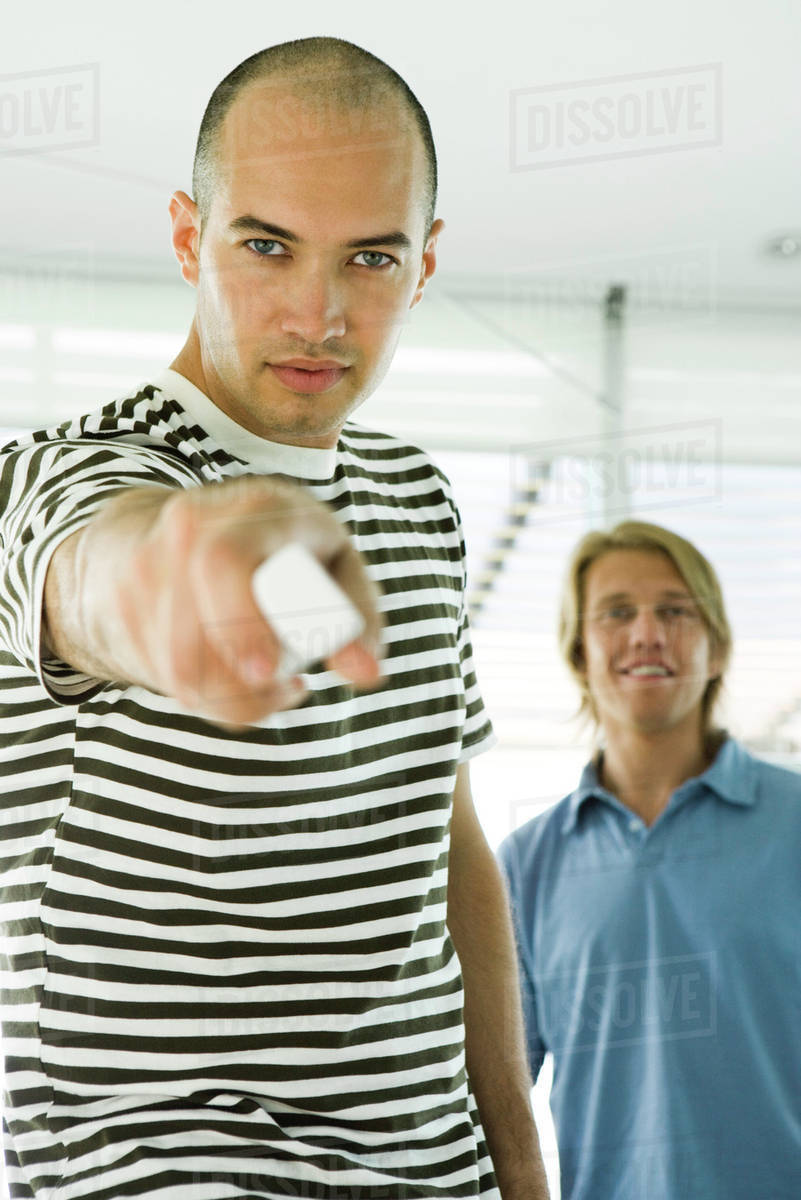 Man pointing remote control at camera, friend standing in background ...