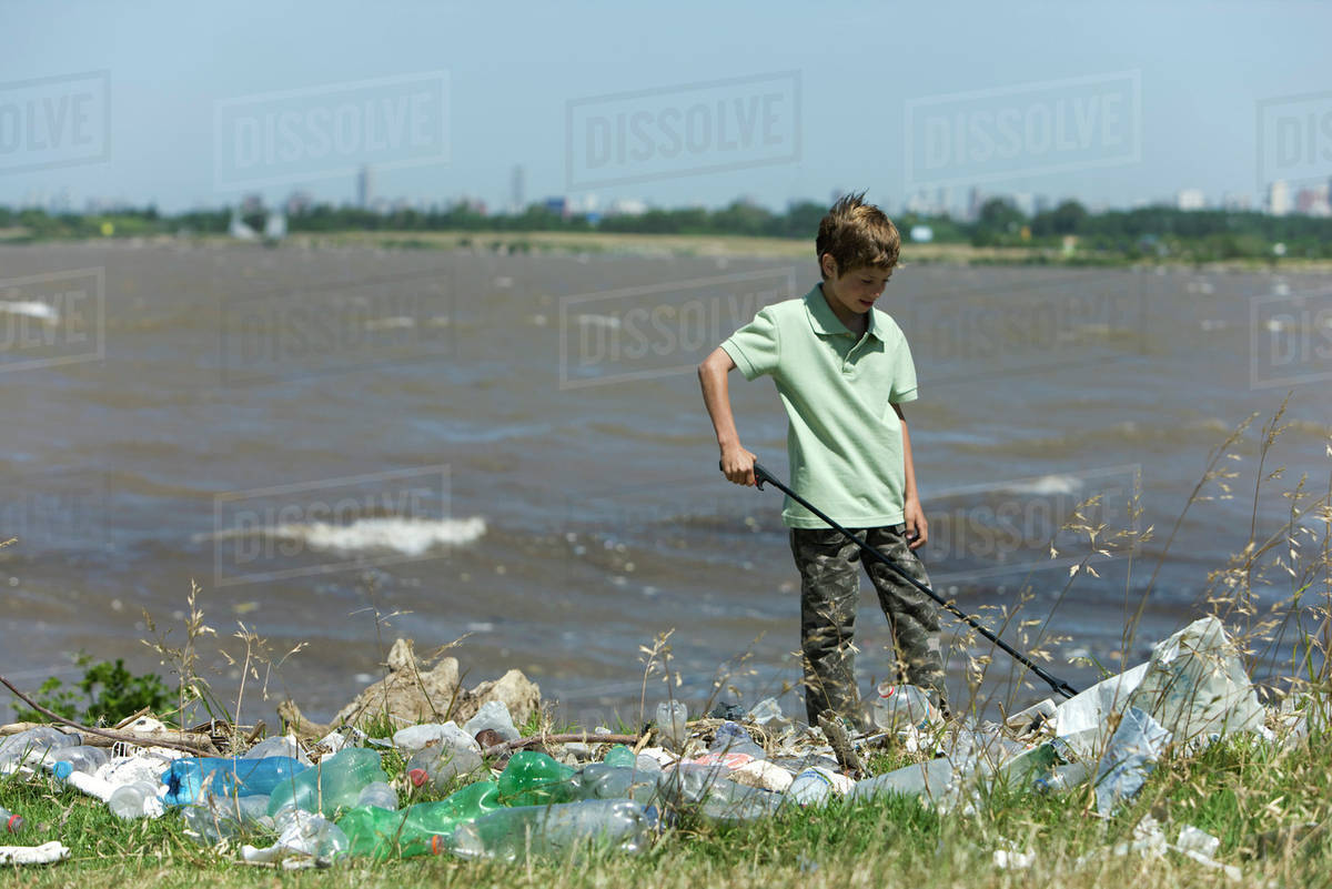 Boy picking up trash on polluted shore - Royalty-free Stock Photo ...