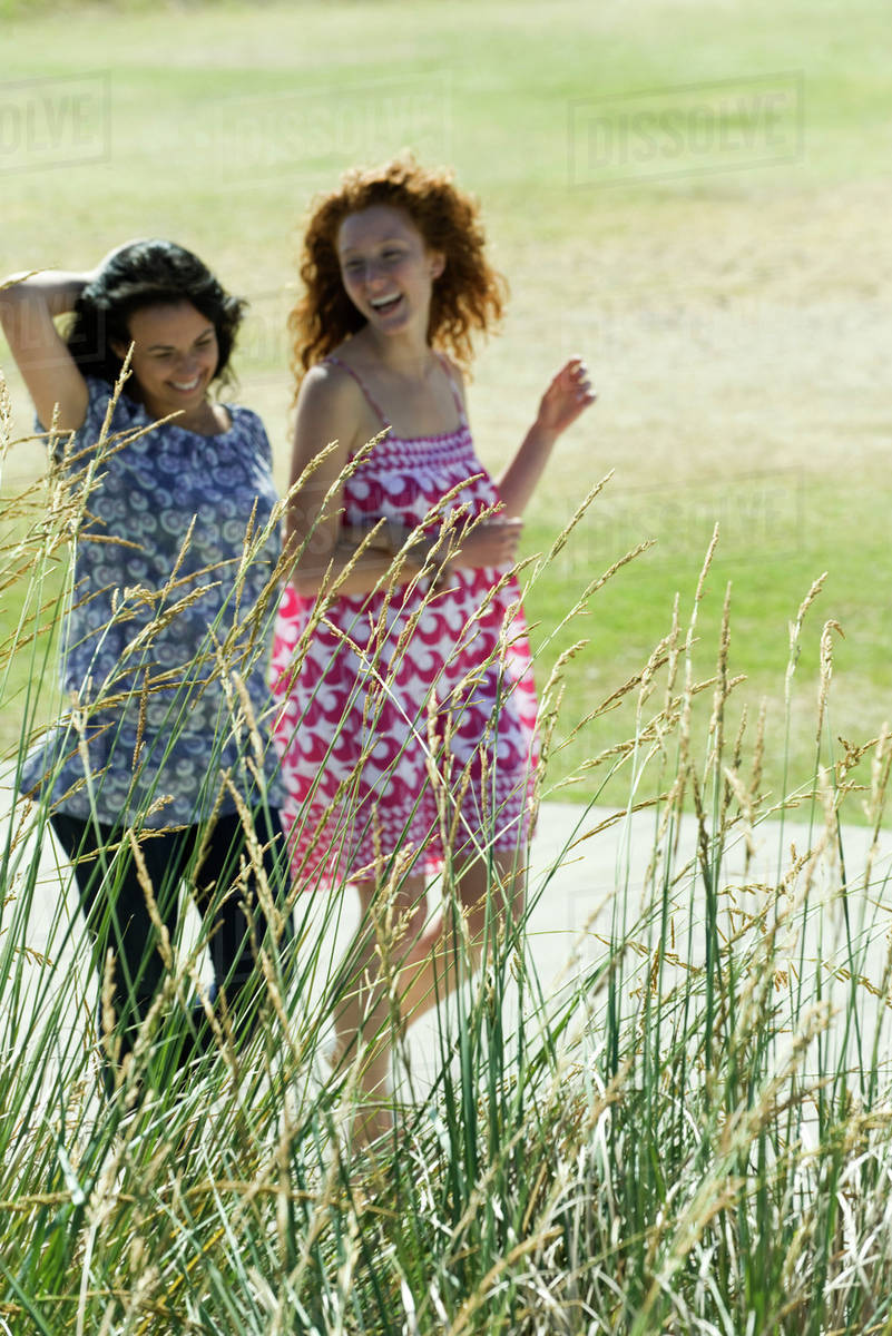 Two young women walking arm in arm outdoors, both laughing - Royalty ...
