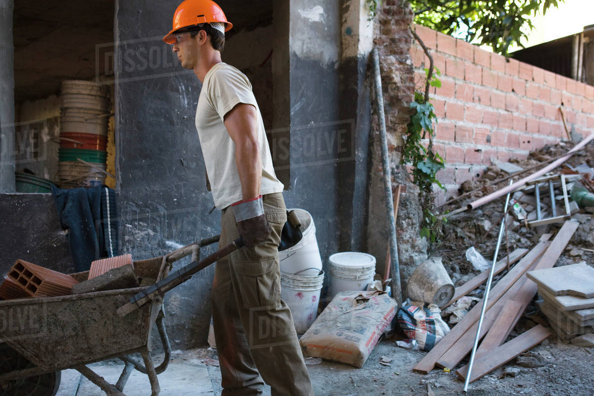 Construction worker moving wheelbarrow through construction site ...