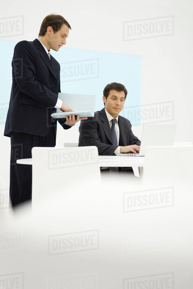 Two businessmen looking at laptop computer together, one holding folder ...