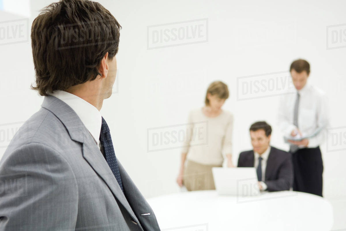 Businessman looking over shoulder at associates in background, close-up ...