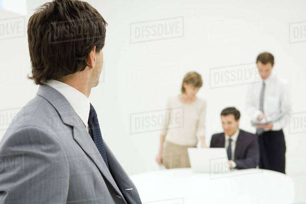 Businessman looking over shoulder at associates in background, close-up ...