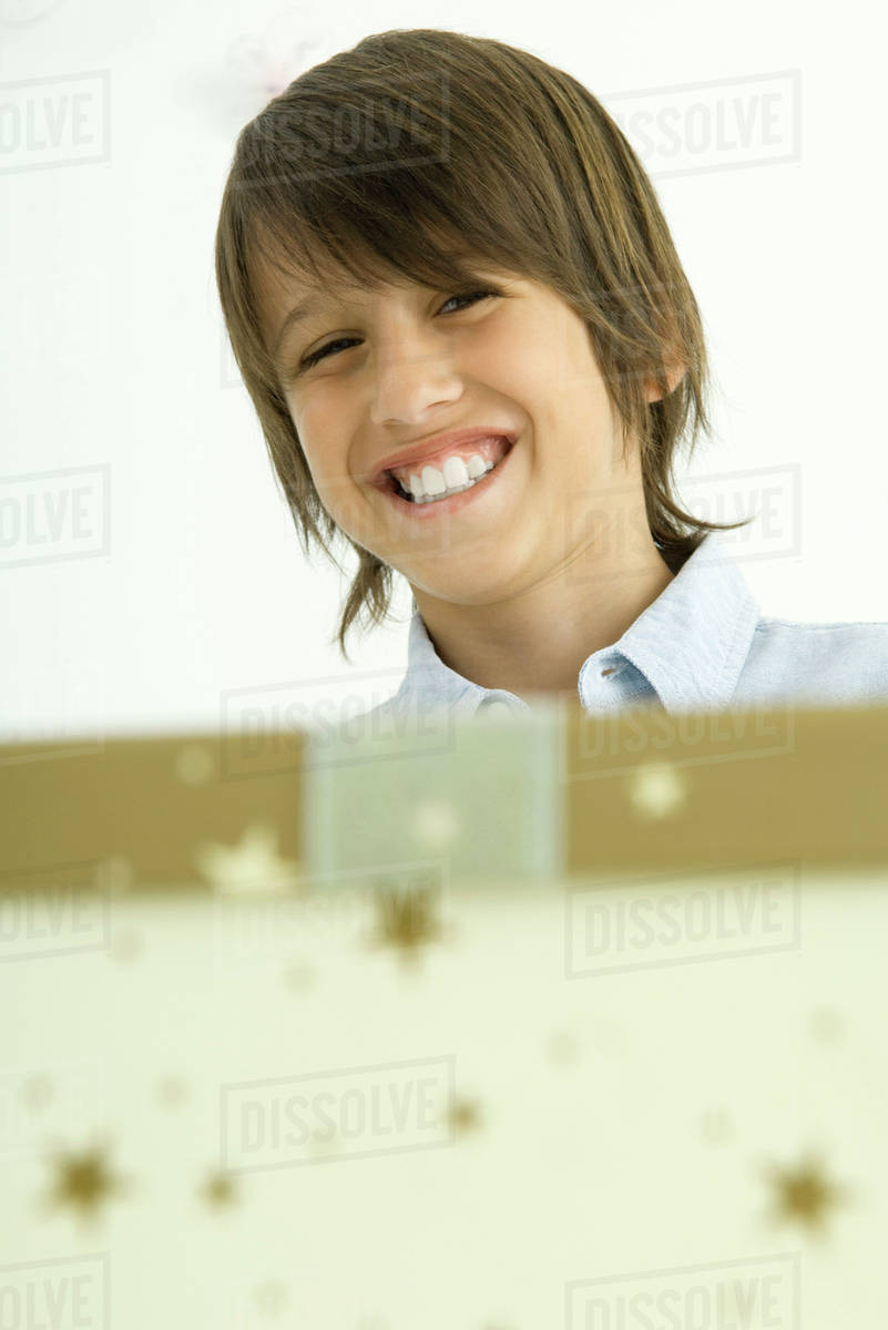 Boy looking over wrapped box, smiling at camera, focus on background ...