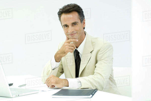 Business executive sitting at desk, smiling at camera, portrait ...