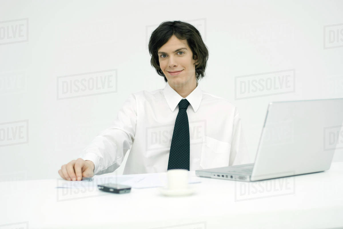 Young professional sitting at desk, smiling at camera - Royalty-free ...