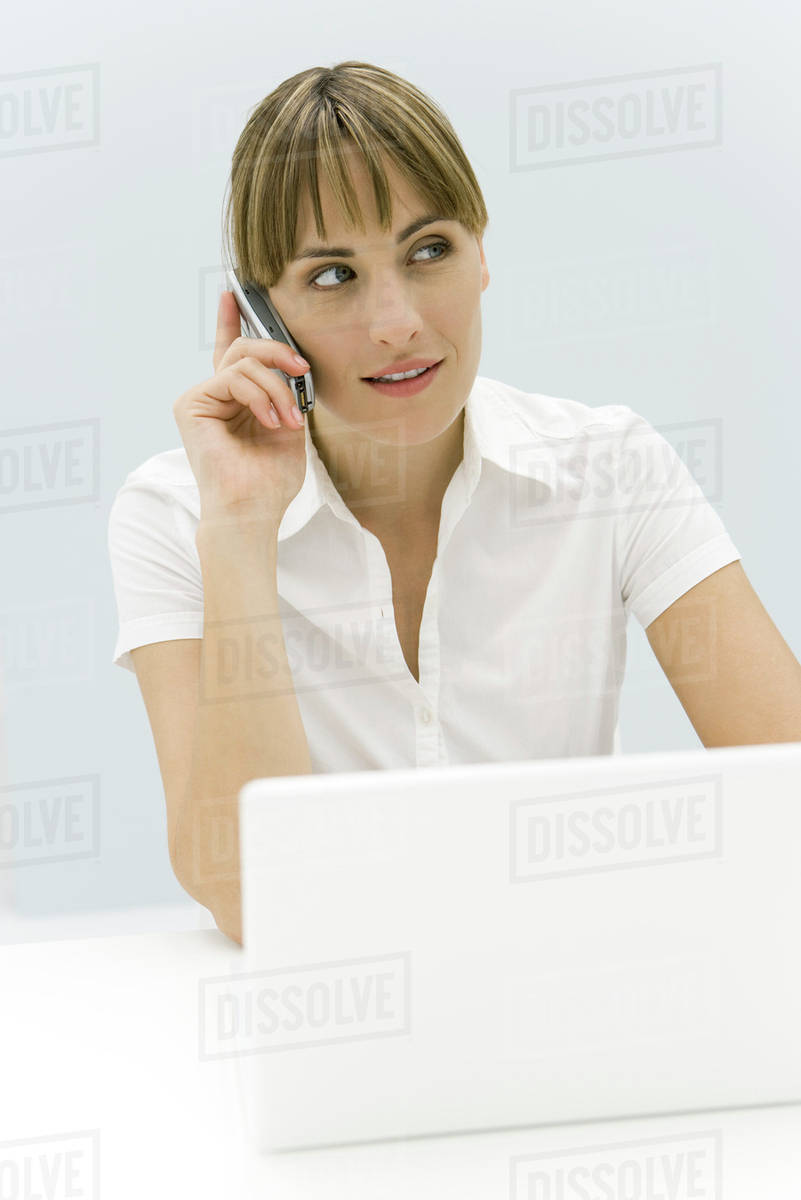Woman sitting in front of laptop computer, using cell phone, looking ...