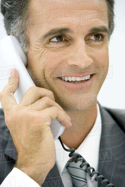 Man using landline phone, smiling, looking away - Stock Photo - Dissolve