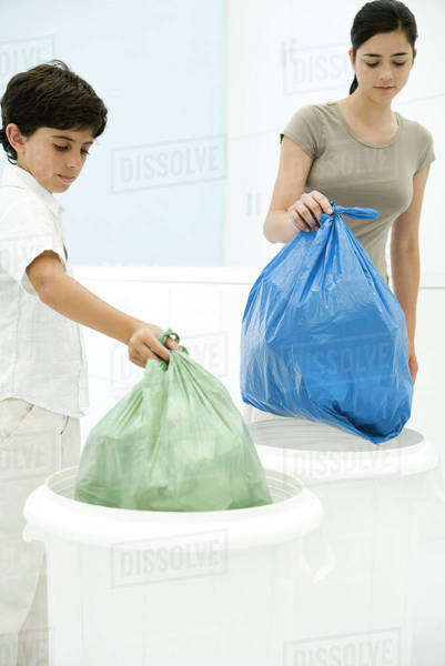 Young woman and boy placing garbage bags in separate garbage cans ...
