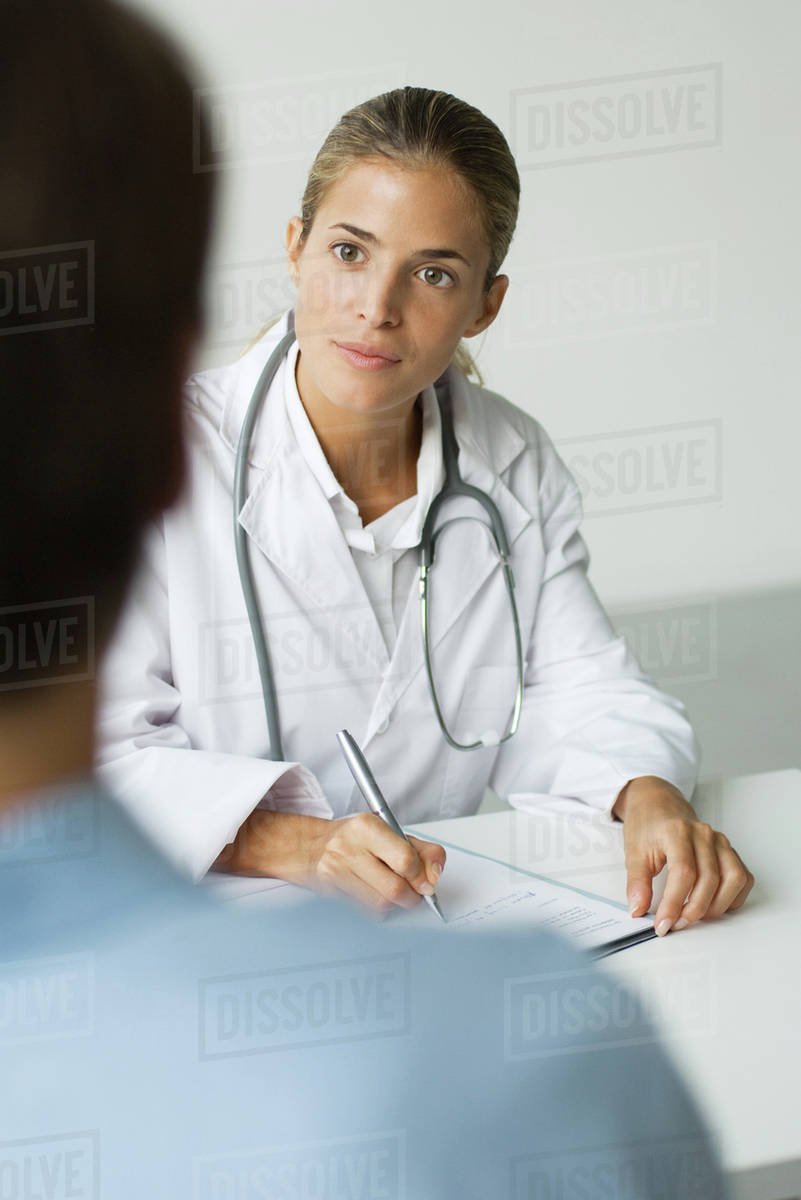 Doctor writing at desk, patient in foreground - Royalty-free Stock ...