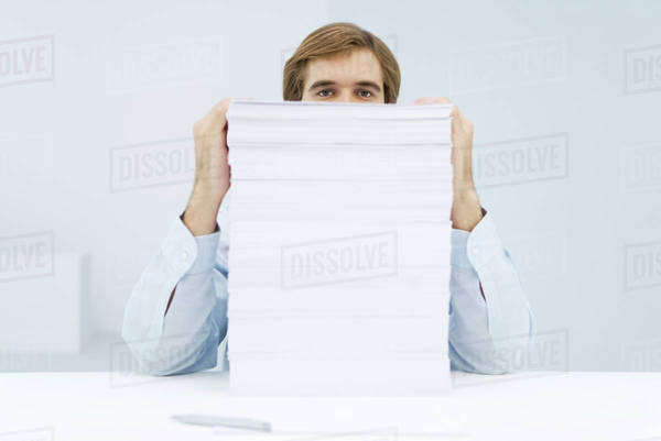 Man peering over tall stack of paper - Stock Photo - Dissolve