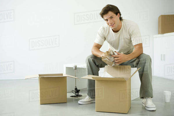 Man unpacking boxes, sitting on bench, smiling at camera - Stock Photo ...