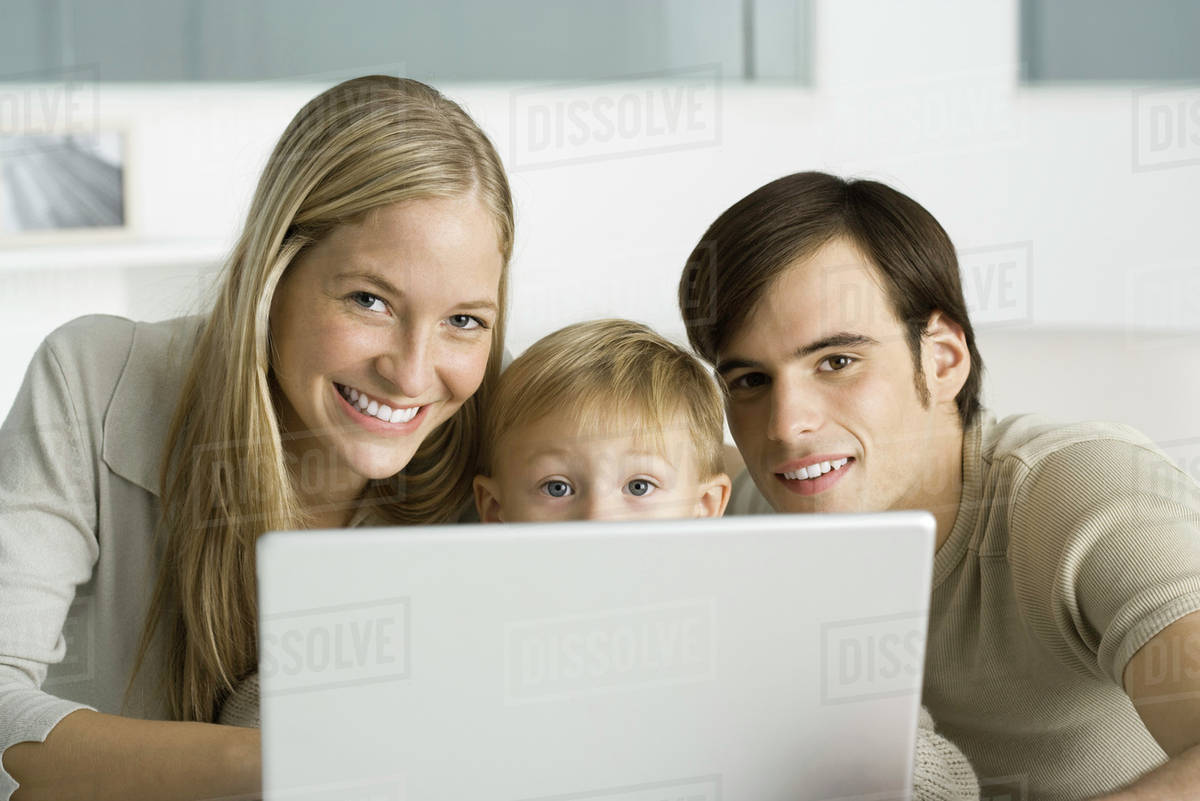 Parents and young son using laptop computer, smiling at camera ...