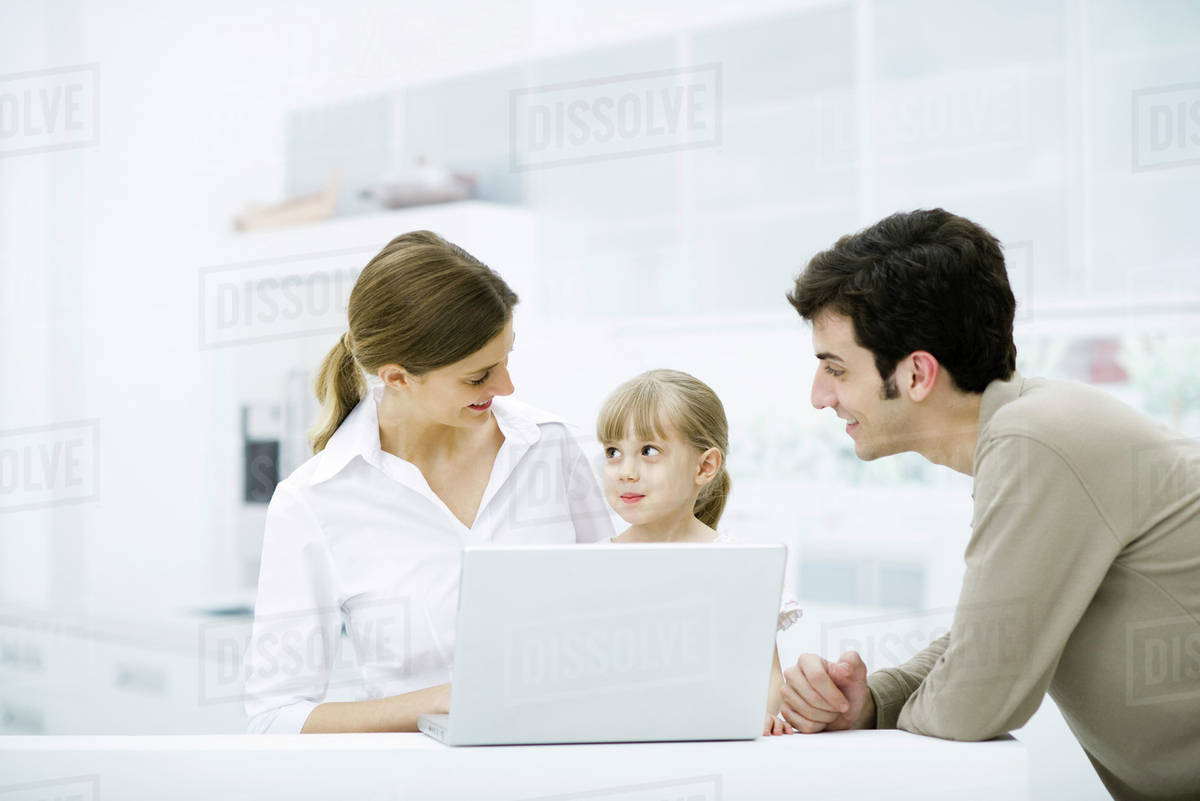 Family gathered around laptop computer, smiling, girl looking at mother ...