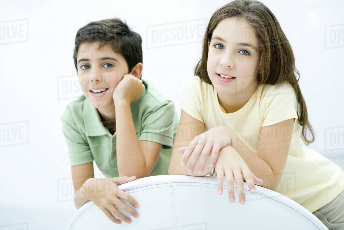 Brother and sister leaning against chair, smiling, portrait - Royalty ...