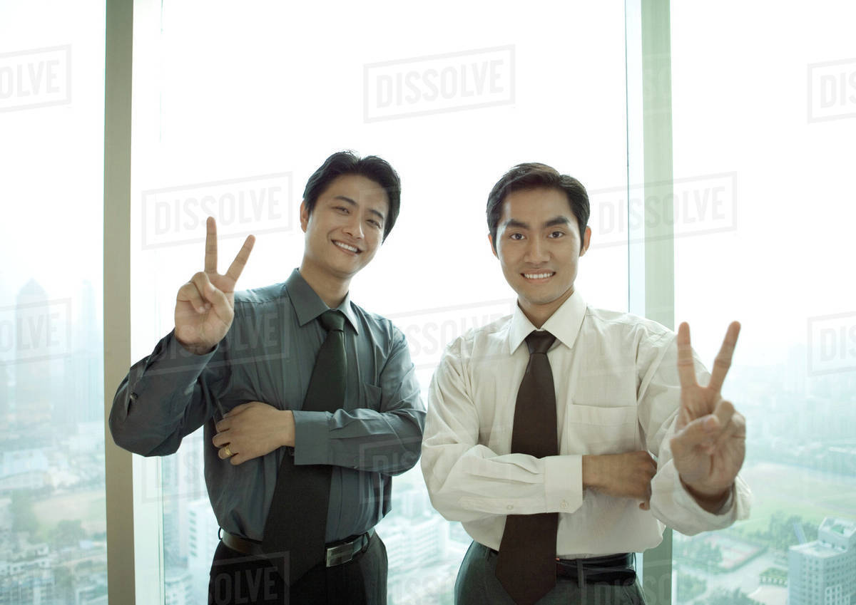 Two businessmen making victory sign, smiling at camera - Stock Photo ...