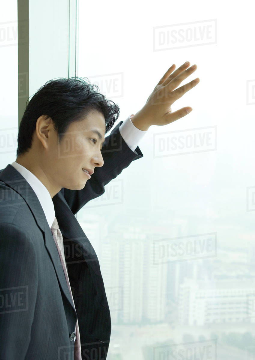 Businessman looking out of window of high rise, side view - Stock Photo ...
