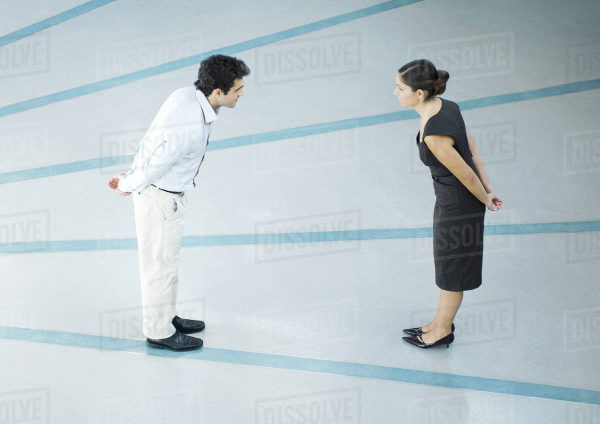 Man and woman standing face to face, hands behind back, leaning toward ...