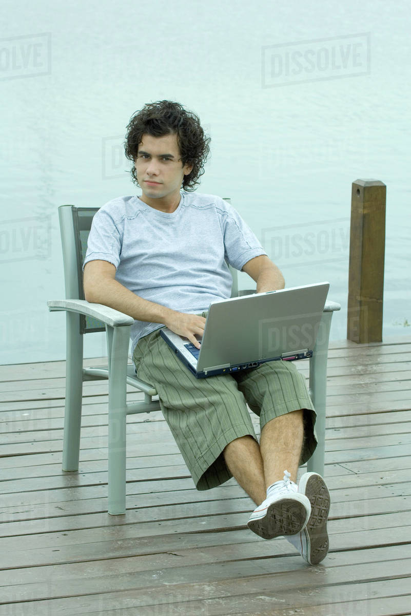 Young man sitting on dock using laptop, full length - Stock Photo ...