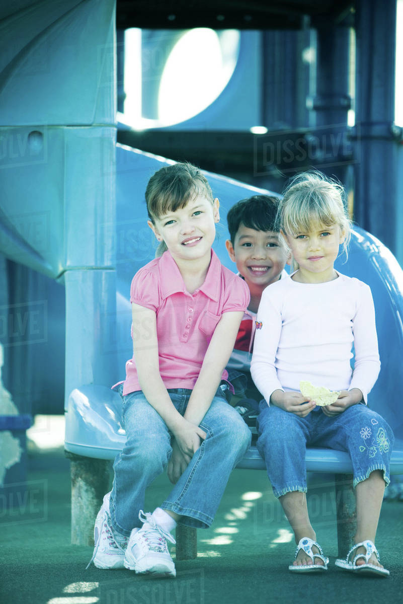 Children sitting on end of slide, smiling at camera - Royalty-free ...
