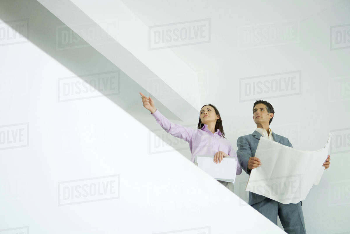 Woman and man standing with blueprints, woman pointing to distance, low ...