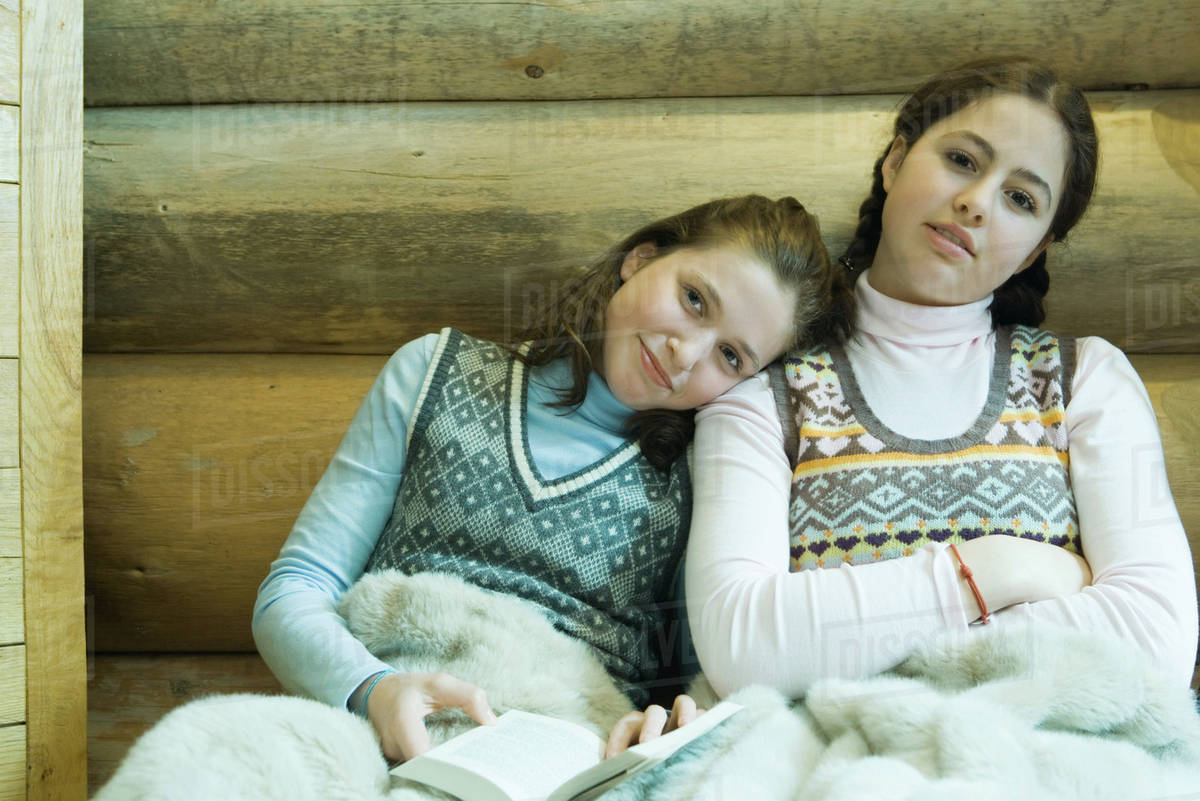 Two teenage girls sharing blanket, smiling at camera, one holding book ...