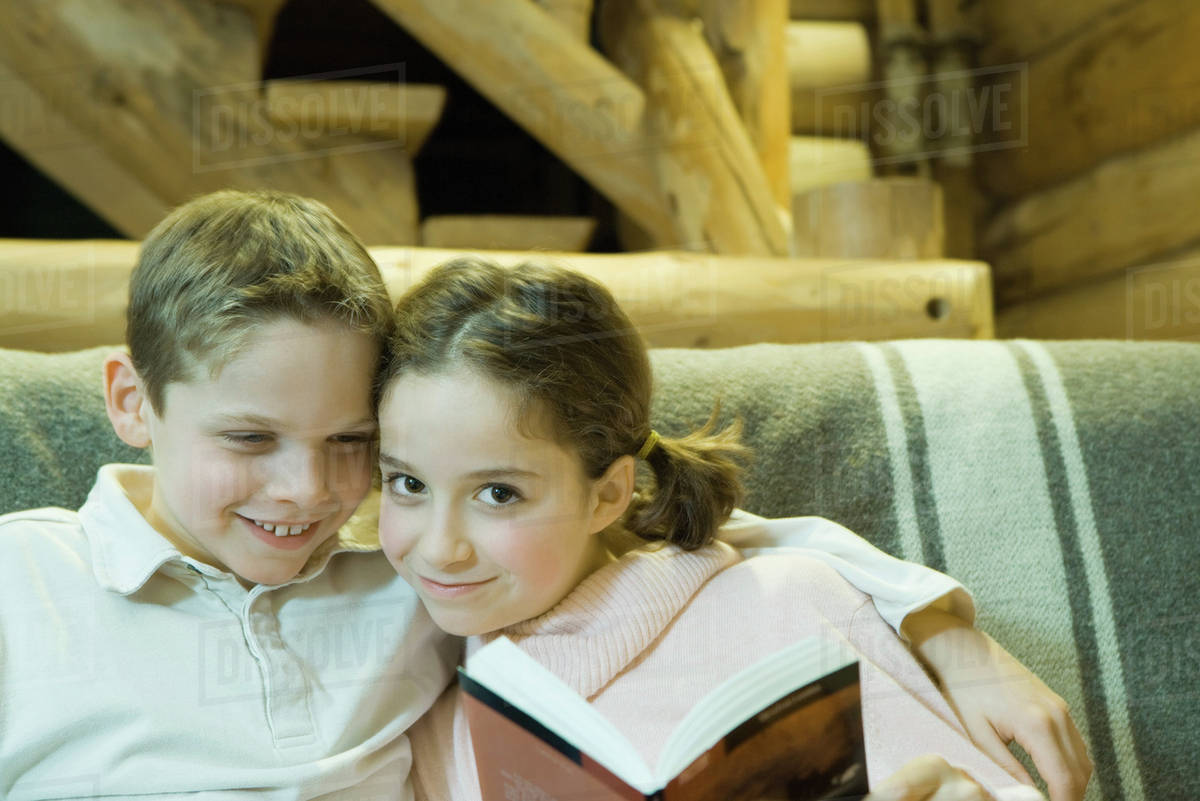 Boy and girl reading together, smiling at camera, cheek to cheek ...