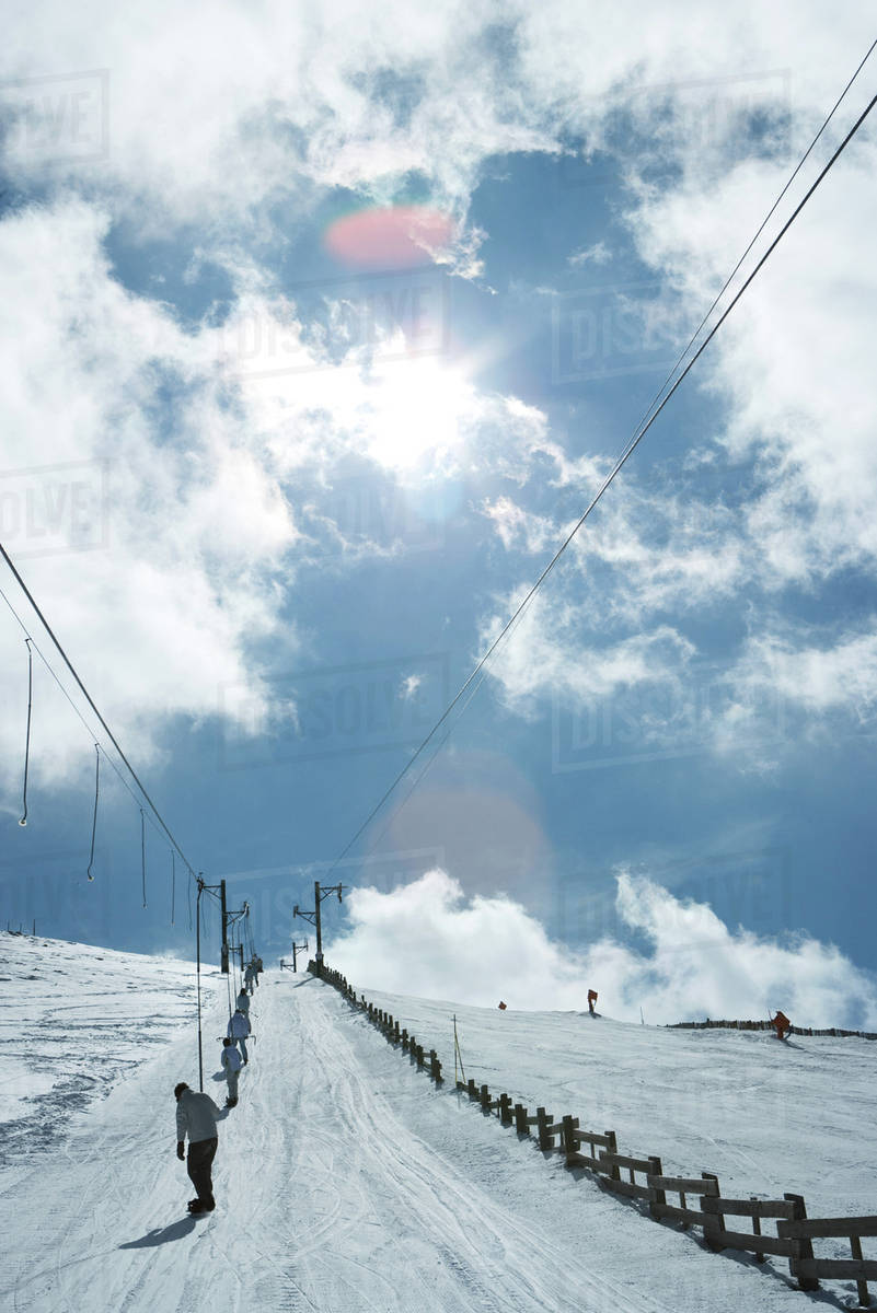 Young skiers using ski lift on hill. rear view, in the distance ...