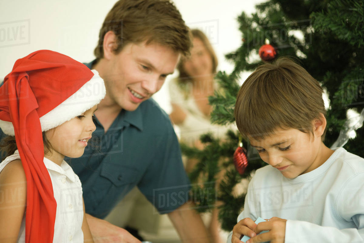 Father and two children opening Christmas present in front of Christmas ...