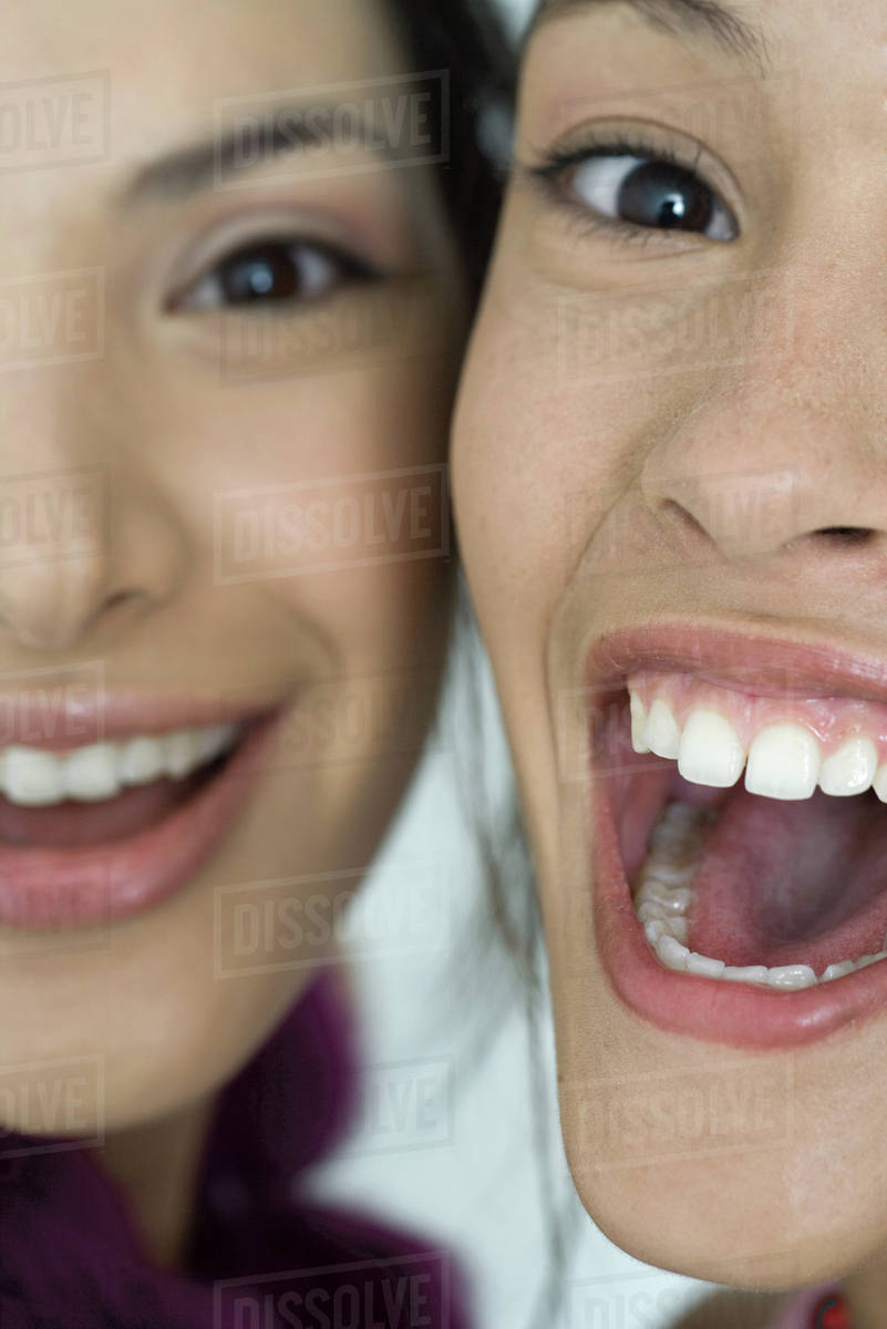 Two young female friends smiling with mouths wide open, looking at ...