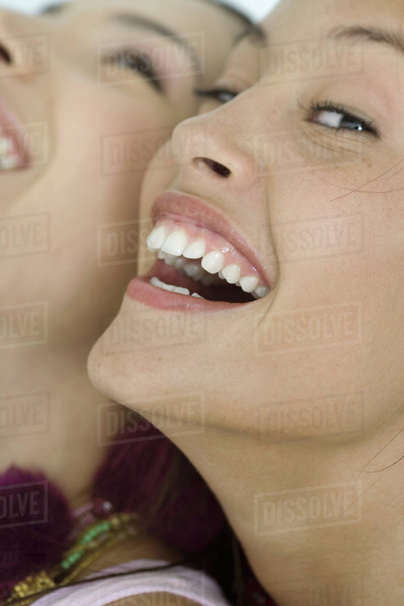 Two young female friends laughing, one looking at camera, extreme close ...
