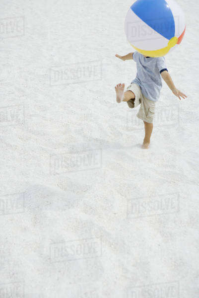 Boy kicking beach ball on beach, head hidden by ball, high angle view ...
