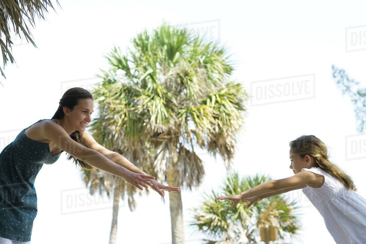 Two sisters reaching toward each other, arms outstretched, low angle ...
