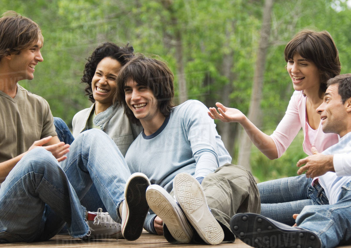 Group of young friends sitting around together outdoors, laughing ...