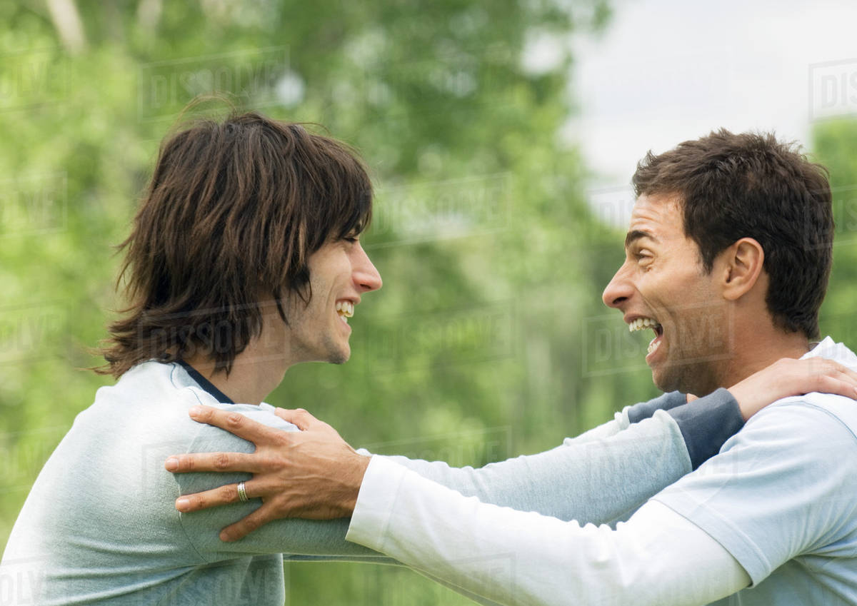 Two young male friends holding each other's shoulders and laughing ...