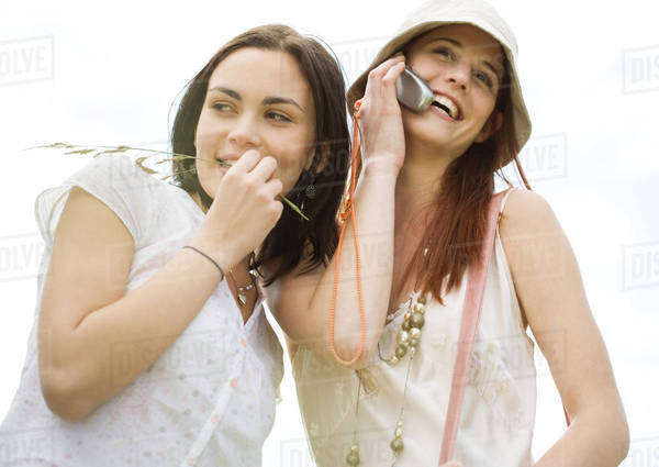 Two young woman outdoors, one using cell phone - Royalty-free Stock ...