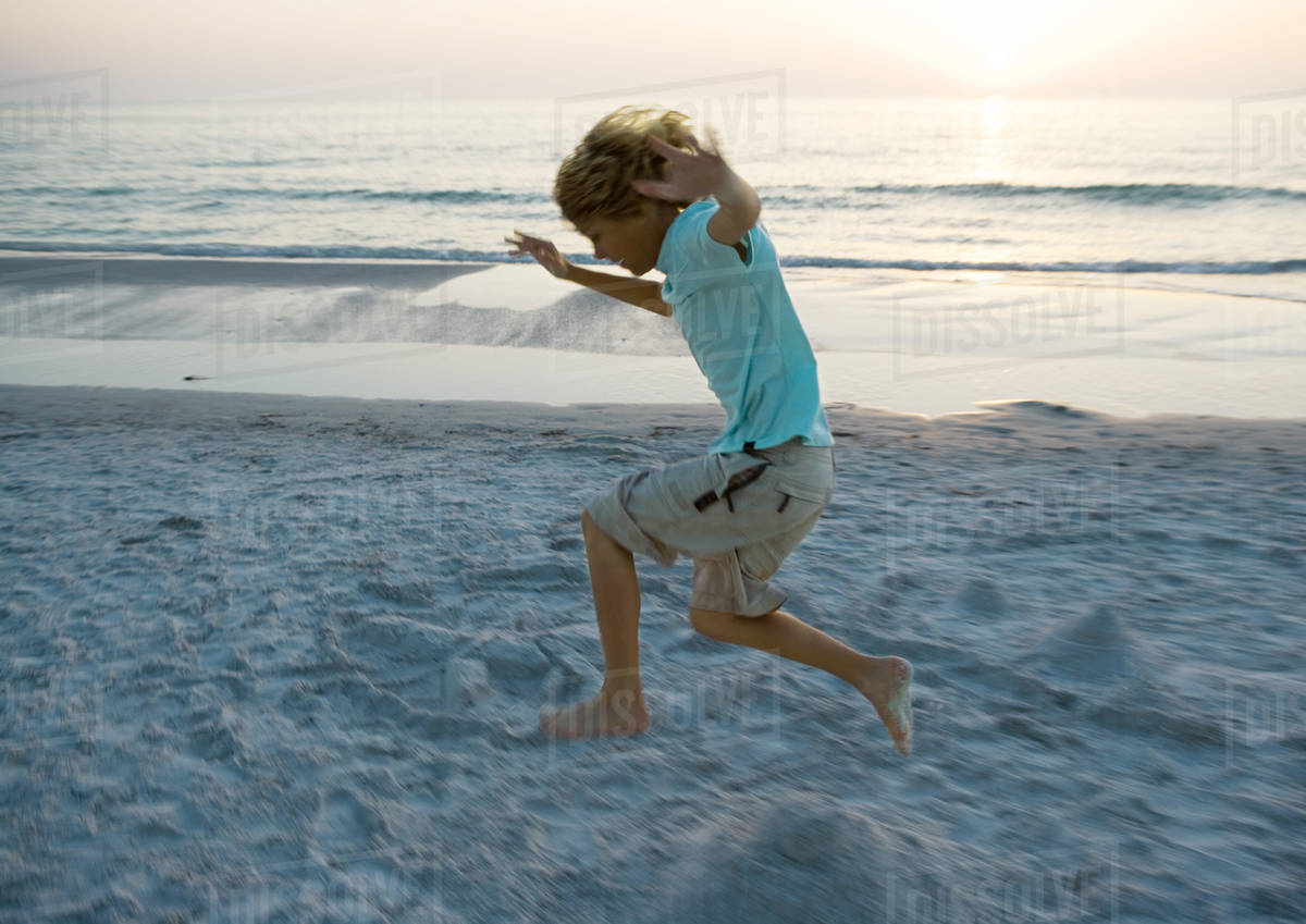 Boy jumping on beach, side view - Royalty-free Stock Photo | Dissolve