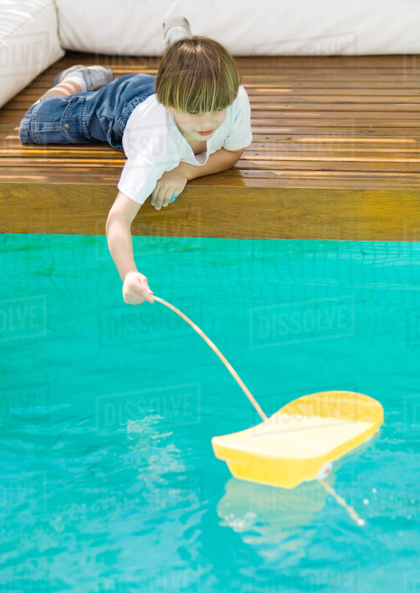 Boy lying on floor near edge of pool, playing with toy boat - Royalty ...