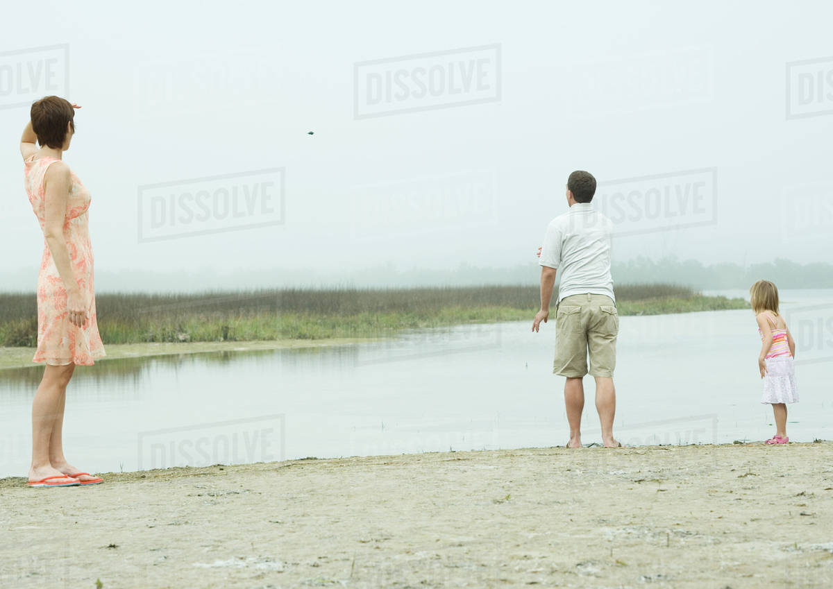 Man throwing pebble into water while family watches - Royalty-free ...