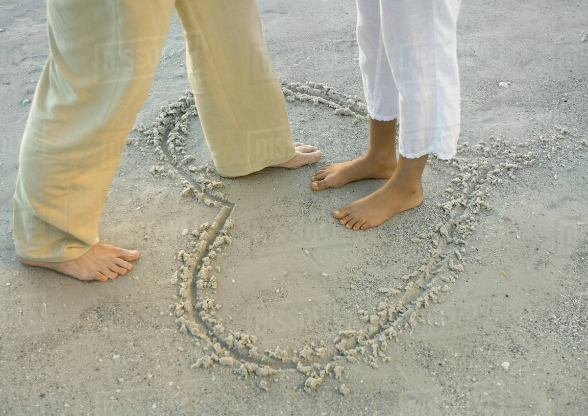 Woman standing in heart drawn in sand, man stepping into heart, view of ...