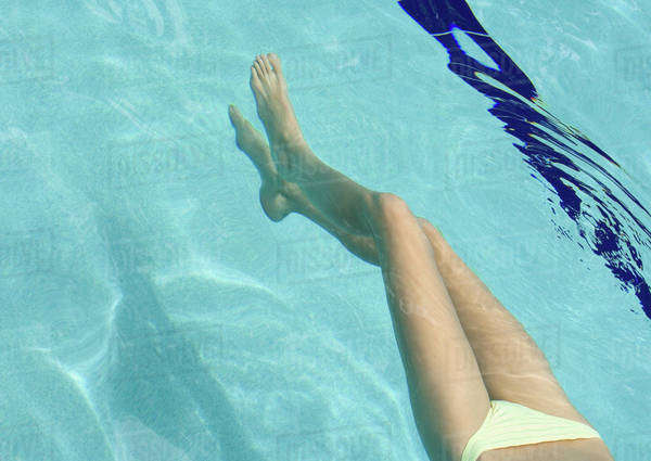 Woman floating in pool, view from waist down - Stock Photo - Dissolve